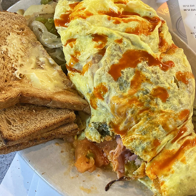 An omelet that refuses to be contained by its plate. Hot sauce zigzags across the top like delicious modern art.