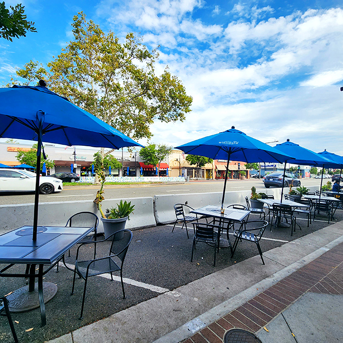 The outdoor seating area, where blue umbrellas create islands of shade for enjoying your pastry treasures under California's perpetually perfect sky.