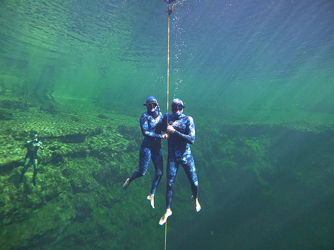 Submerged in otherworldly blue, divers experience weightless exploration of ancient limestone formations shaped by millennia of flowing water.