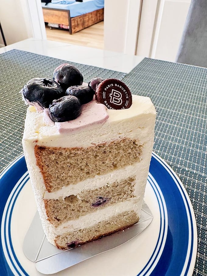 This blueberry chiffon cake slice reveals perfect layers that would make a geologist weep – light, airy cake strata supporting fresh berries and cream that defy gravity.