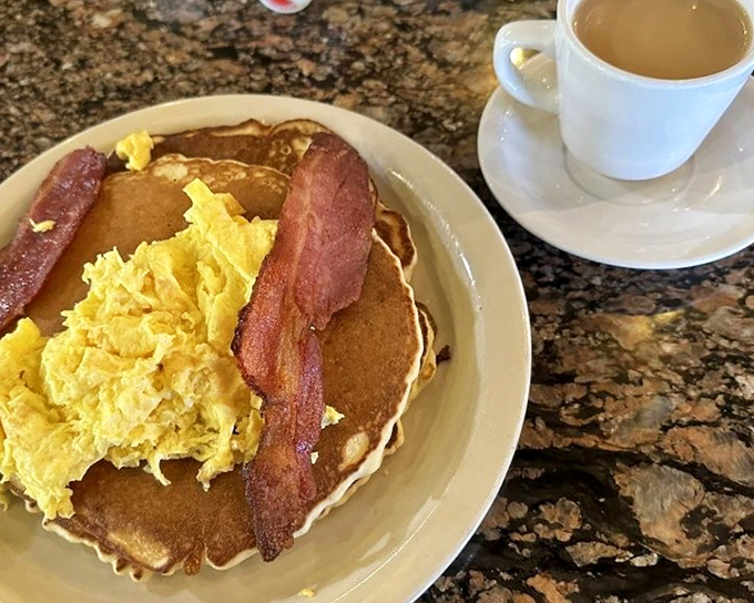 The breakfast trifecta: golden pancakes, perfectly scrambled eggs, and bacon that's achieved that magical balance between crisp and chewy.