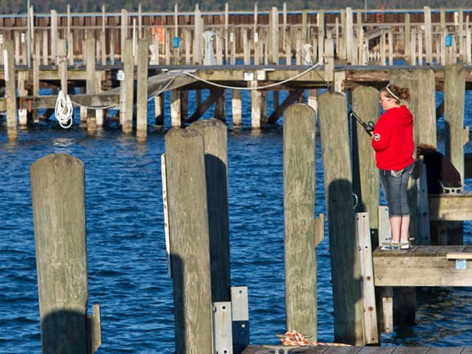 Wooden pilings create a rhythm in the calm waters of East Tawas Marina. A solitary figure in red enjoys the meditative act of fishing&mdash;proof that the best things in life aren't things.