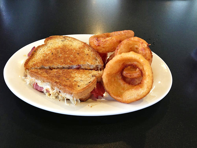 The Reuben—architecture in sandwich form. Those onion rings aren't just a side dish; they're a statement piece that completes the composition.