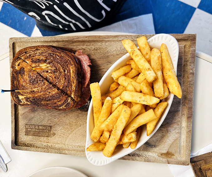 A perfectly grilled Reuben sandwich shares wooden board space with seasoned fries&mdash;simple food elevated to art through decades of practice.