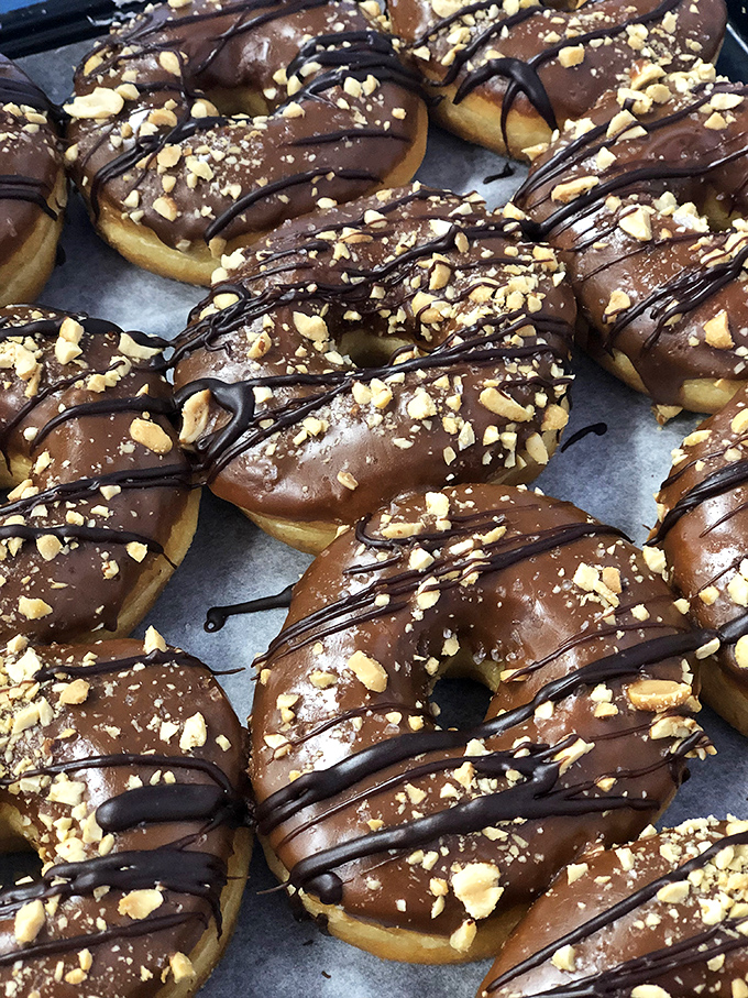Chocolate-glazed donuts with peanuts and chocolate drizzle &ndash; proof that sometimes more is more, especially when it comes to toppings.