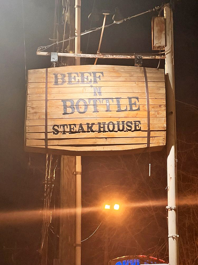 By night, this wooden sign becomes a beacon for hungry travelers, promising relief from chain restaurant mediocrity just ahead.