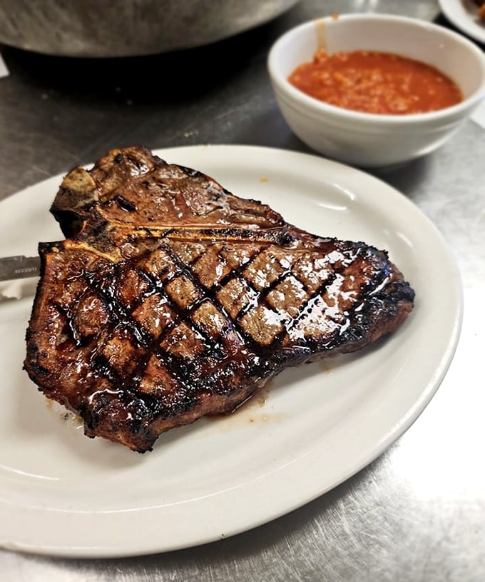 A T-bone steak with perfect grill marks that would make backyard barbecue champions question their life choices. Carnivorous poetry on a white plate.