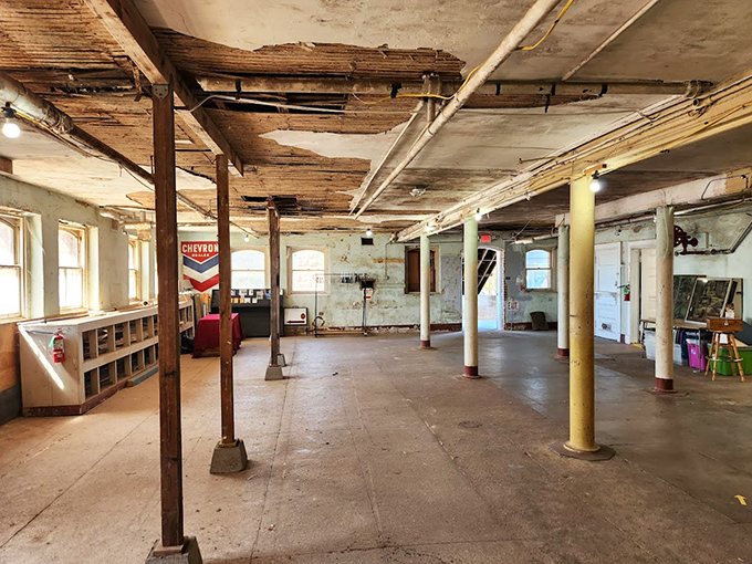 Sunlight filters through tall windows into this vast open space, where support columns stand like sentinels guarding the memories of a building slowly returning to nature.