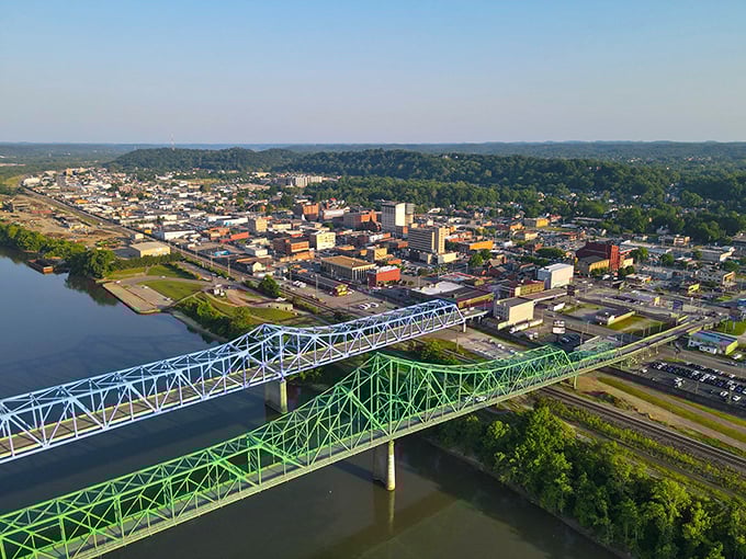 An aerial view reveals Ashland nestled between the Ohio River and rolling hills. The blue and green bridges connect Kentucky to Ohio like colorful friendship bracelets.