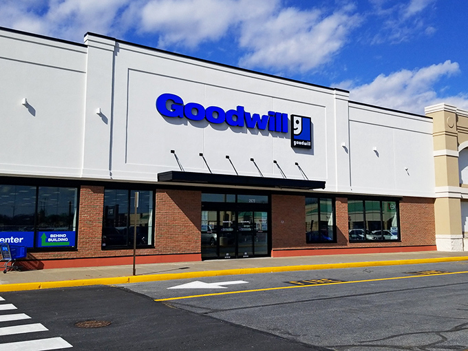 The Goodwill storefront stands ready like a treasure chest waiting to be opened. Blue sign gleaming with promise of undiscovered bargains inside.