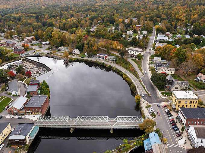 Bird's eye perfection! The village unfolds like a miniature model town, with the iron bridge connecting two worlds across the glassy river.