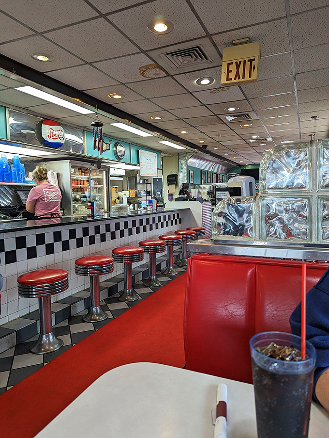 Classic red vinyl stools line the checkered counter where culinary dreams come true. The glass block wall adds that perfect mid-century touch to your dining experience.