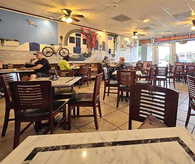 Warm wooden chairs and marble-topped tables create an inviting atmosphere, while framed images of Greek landscapes transport you across the Atlantic