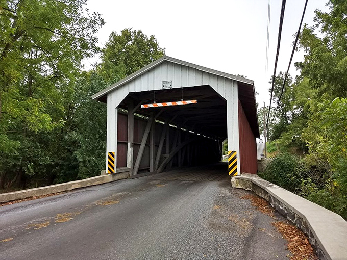 A classic covered bridge stands as a time portal between eras, its wooden bones sheltering travelers just as it has for generations.