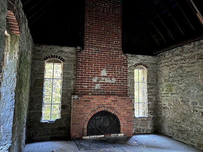 The castle's magnificent brick fireplace stands as a silent witness to history, framed by tall windows that bathe the empty room in dancing light.