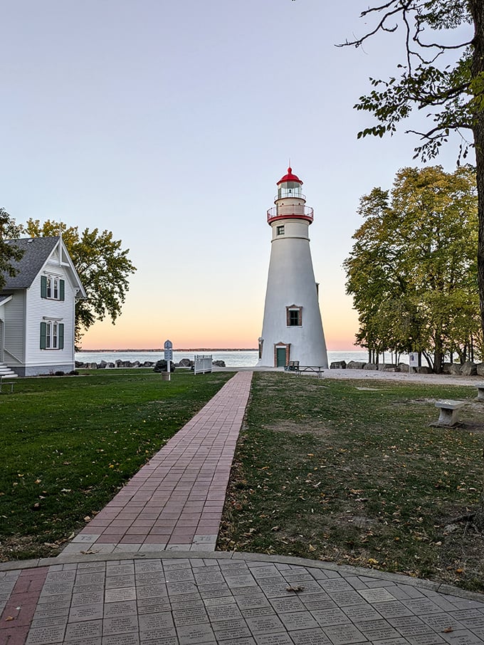 The brick pathway invites visitors toward maritime history, with the keeper's house standing sentinel alongside its towering neighbor at sunset.