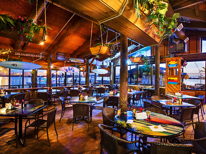 Rustic wooden beams and hanging plants create the perfect backdrop for waterfront dining. The sunset views through those windows? Absolutely free with every meal.