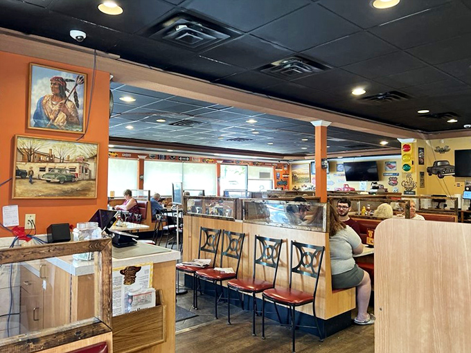 Orange walls and vintage artwork create that perfect small-town diner atmosphere where conversations flow as freely as the coffee refills.