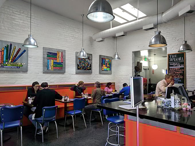 Inside, bright orange booths pop against white walls adorned with colorful artwork &ndash; where industrial-chic meets retro diner comfort in perfect harmony.