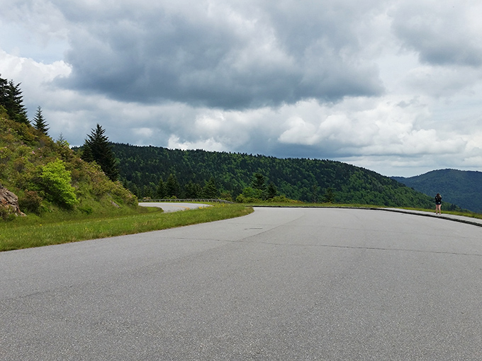 The road curves like nature's welcome mat, inviting travelers to pause where dramatic clouds play hide-and-seek with mountain peaks.