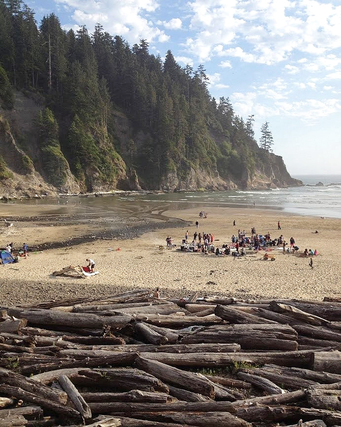 Where forest meets ocean in perfect harmony – towering cliffs stand guard while beachgoers create memories on this hidden crescent of paradise.