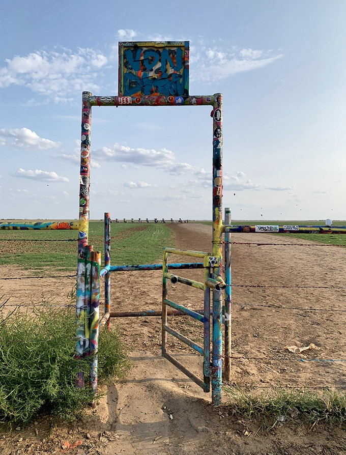 This colorful gateway stands as the unofficial entrance to automotive heaven. The graffiti-covered frame perfectly frames the distant buried cars.