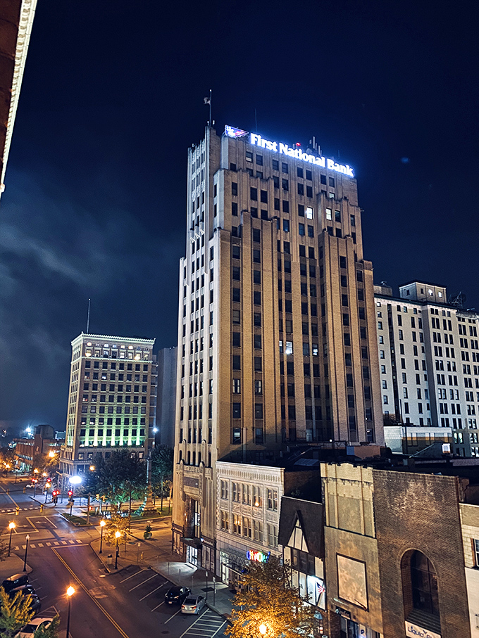 Youngstown's downtown buildings light up as night falls, transforming the cityscape. The First National Bank tower stands like a golden sentinel watching over the streets below.