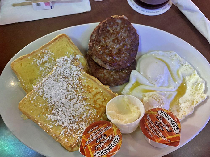 French toast dusted with powdered sugar alongside savory sausage patties and perfectly cooked eggs &ndash; breakfast harmony on a plate.