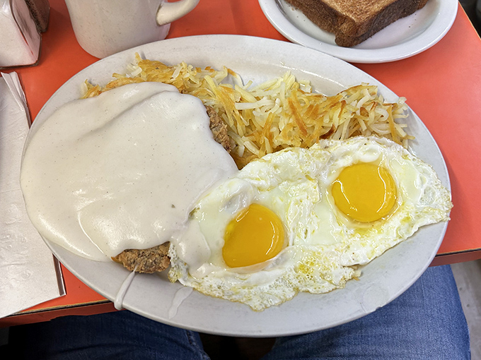 Sunny-side up eggs with perfect golden yolks stand guard over a mountain of hash browns. Breakfast architecture at its finest.