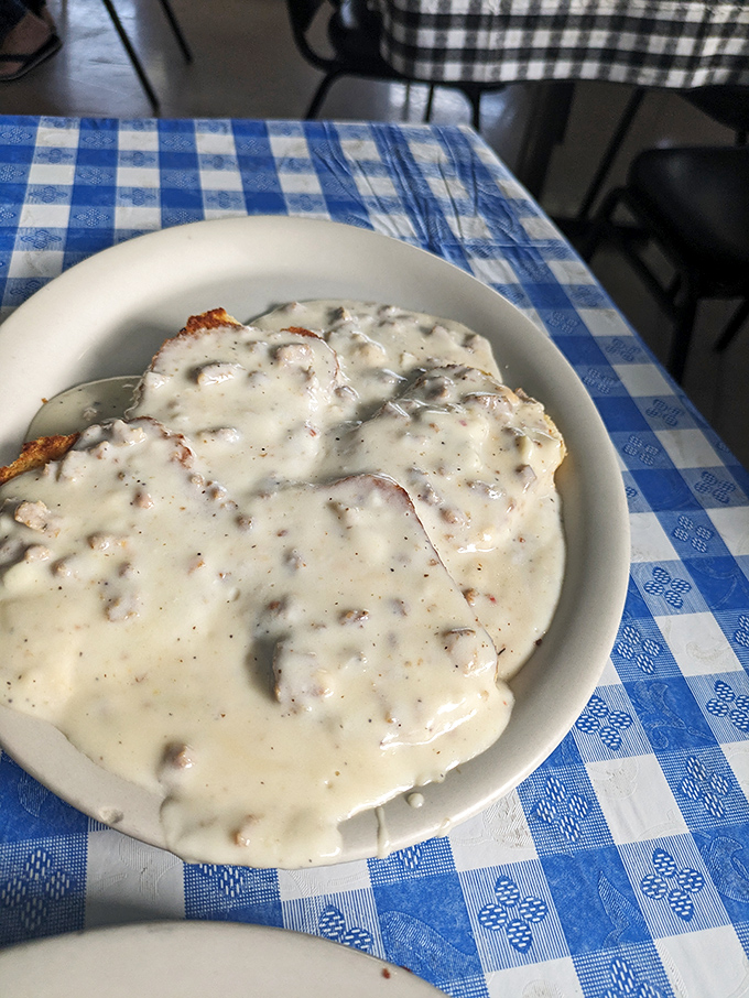 Biscuits and gravy that would make your Southern grandmother nod in approval—creamy, peppery perfection on a blue-checked tablecloth.