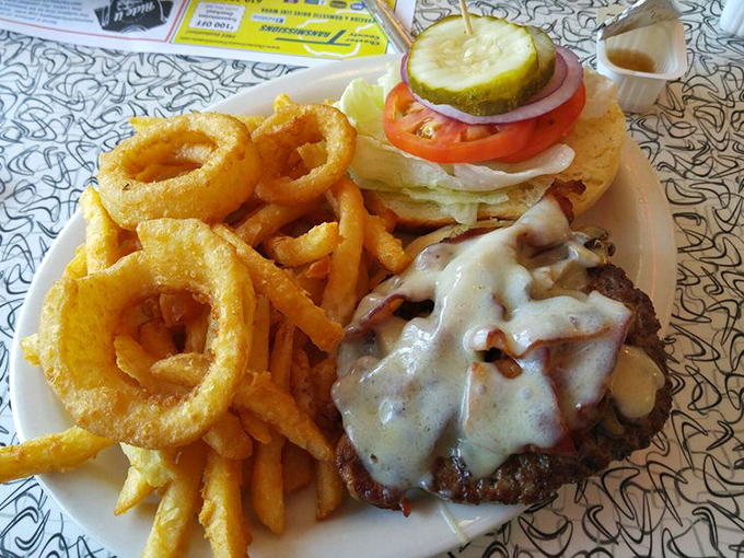 The burger arrives like a cheesy volcano eruption, with crispy onion rings standing guard. Diet plans enter at their own risk.
