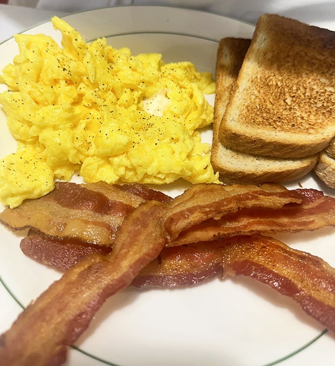 Sunshine on a plate: perfectly scrambled eggs, toast with that ideal golden-brown hue, and bacon that's achieved the mythical balance between crispy and chewy.