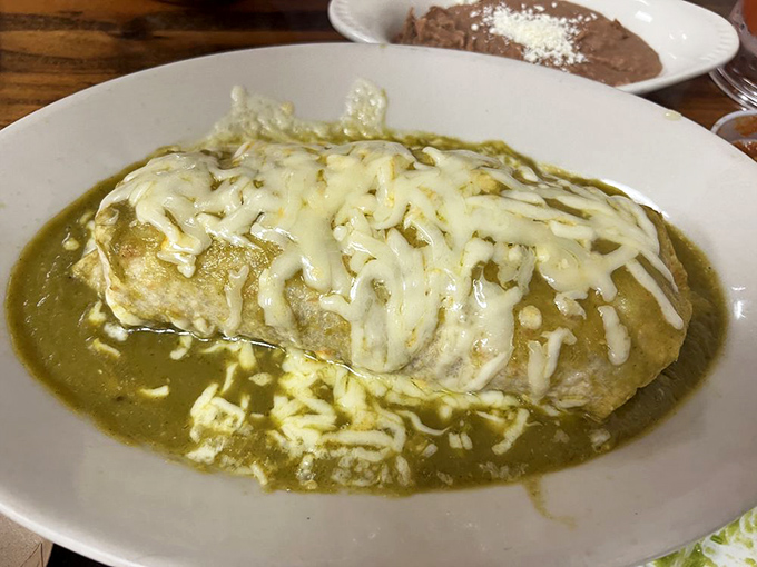 Behold the burrito in its natural habitat: swimming in vibrant green salsa, blanketed with melted cheese, waiting to fulfill its destiny.