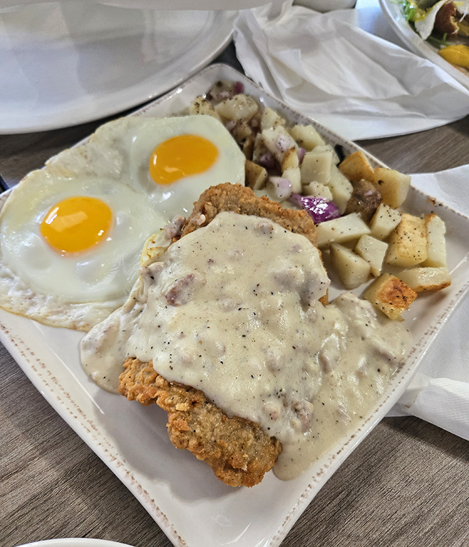 The legendary chicken fried steak in all its glory &ndash; golden crispy exterior, smothered in peppery gravy, with sunny-side eggs standing guard. This is breakfast nirvana.