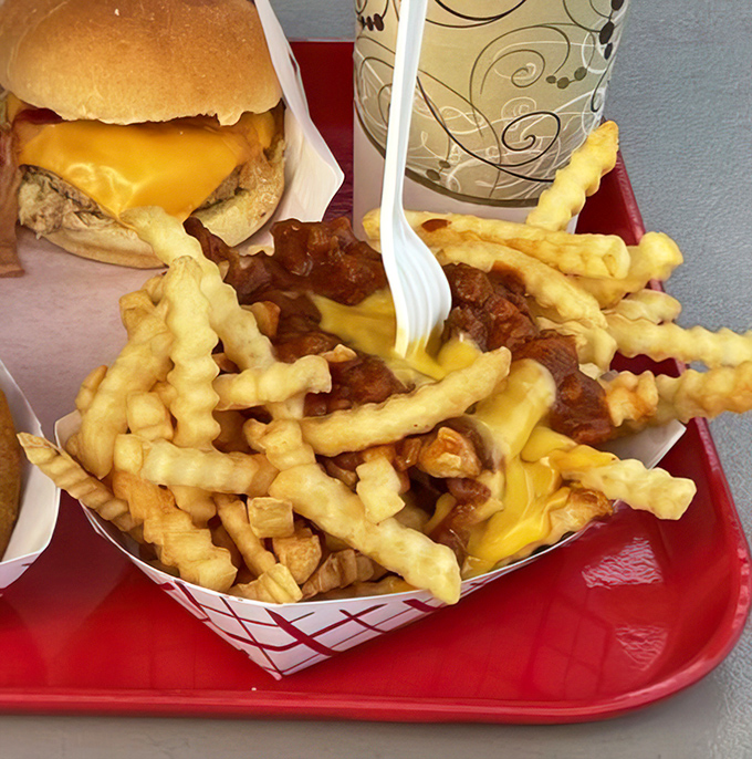 Crispy, golden crinkle-cut fries smothered in savory chili and melted cheese, sitting beside a perfectly crafted cheeseburger. Diet starts tomorrow!