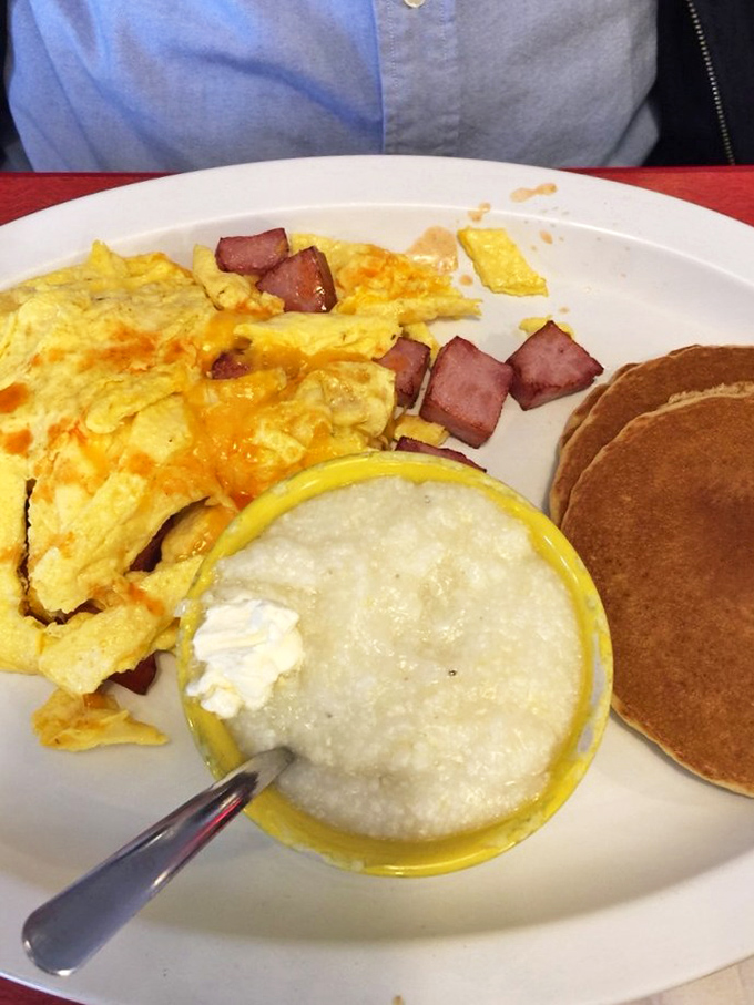 A perfect breakfast trinity: fluffy scrambled eggs with ham, creamy grits with a pat of butter, and pancakes waiting for syrup.