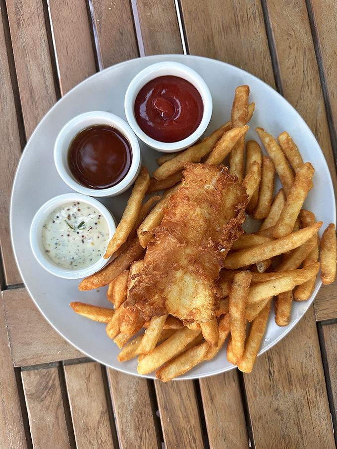 Golden-battered fish perched atop a mountain of crispy fries. Three dipping sauces because life's too short for condiment monogamy.
