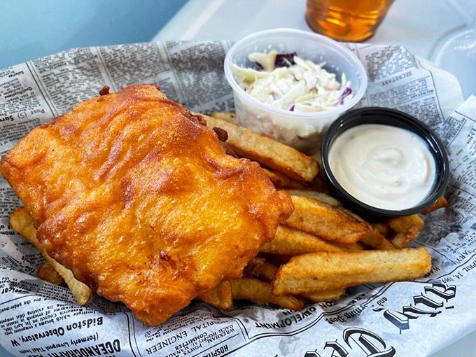 Golden-battered fish resting on a bed of chips, with coleslaw and tartar sauce standing by. This isn't just food; it's edible sunshine.