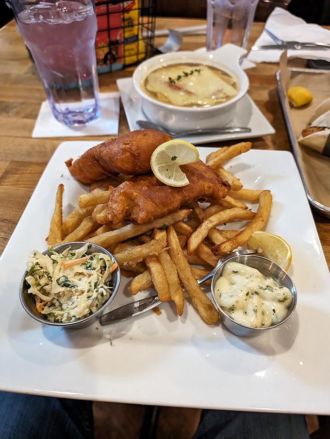 Golden-battered fish resting on a bed of crispy fries, accompanied by creamy coleslaw and house-made tartar sauce &ndash; the holy trinity of fish and chips perfection.