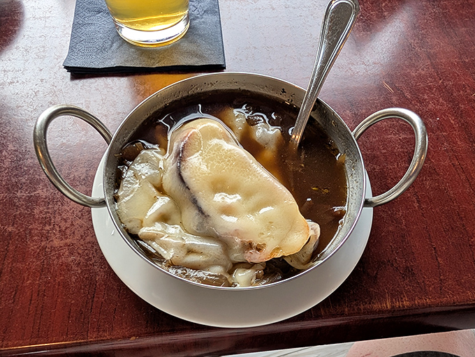 The legendary French onion soup arrives like a cheese-capped superhero, ready to save you from mundane dining experiences one glorious spoonful at a time. 