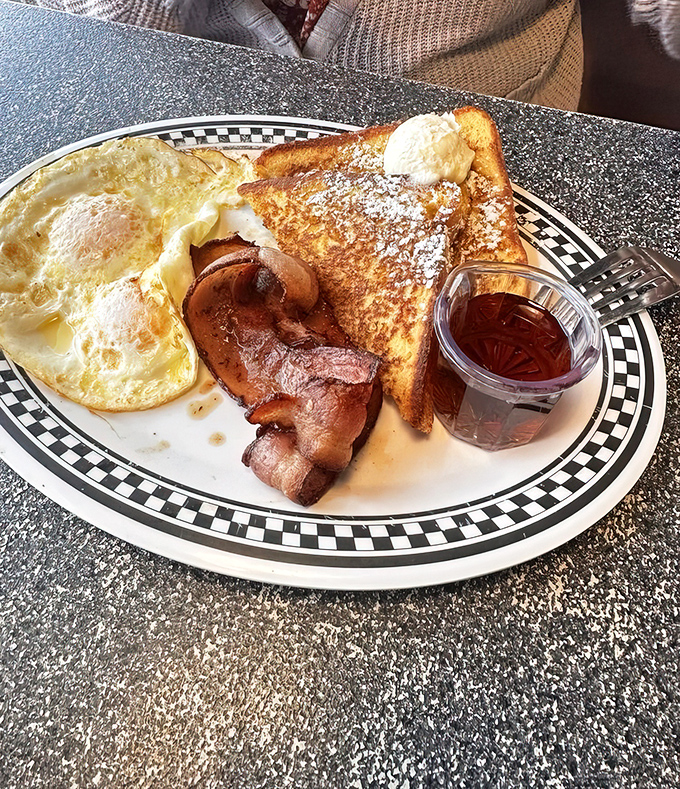 The holy trinity of breakfast: golden French toast dusted with powdered sugar, perfectly cooked eggs, and bacon that would make vegetarians question their life choices.