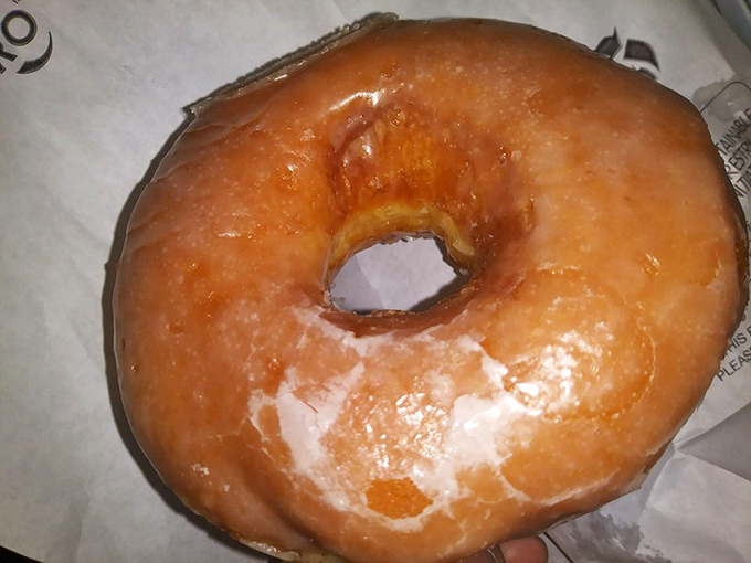 Behold the glazed masterpiece—a perfect golden ring with that signature glassy sheen that shatters like sugar crystal armor with each bite.