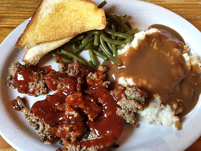 Behold the star attraction: meatloaf that doesn't just sit on the plate but commands it, flanked by green beans and mashed potatoes drowning happily in gravy.