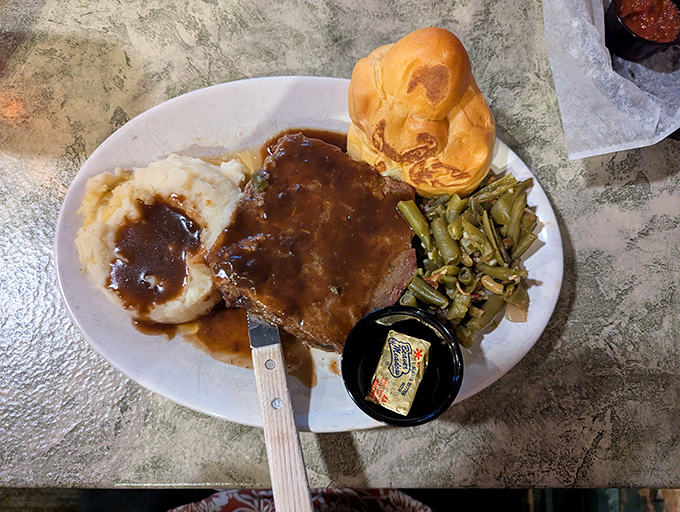 Behold: the meatloaf that launched a thousand road trips. That gravy river flowing into mashed potato mountain is pure Midwestern poetry.