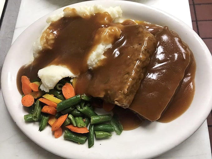 Behold, the legendary meatloaf in its natural habitat &ndash; swimming in savory brown gravy, nestled against cloud-like mashed potatoes and colorful vegetables.