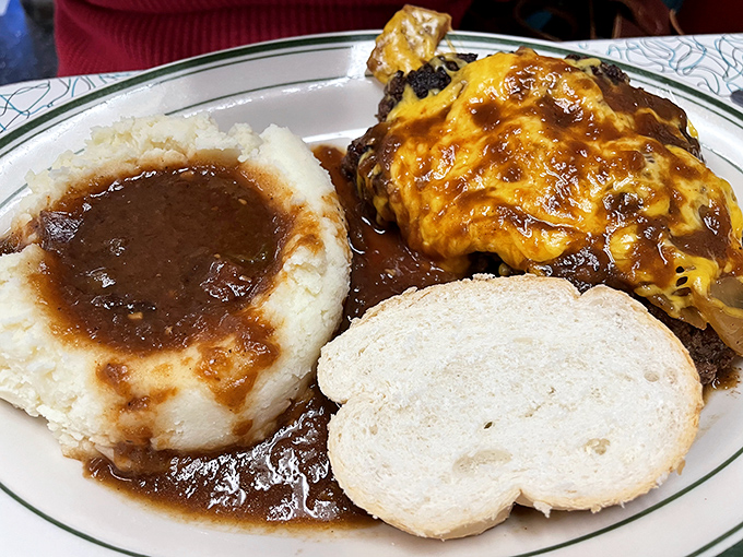 Behold the star attraction: meatloaf crowned with melted cheese, swimming in rich gravy alongside cloud-like mashed potatoes and a humble slice of bread.