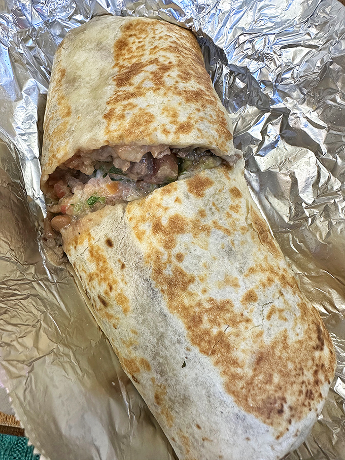 Behold the Mission-style masterpiece in its foil throne. Golden-spotted tortilla cradling a perfect ratio of meat, beans, and fresh salsa.