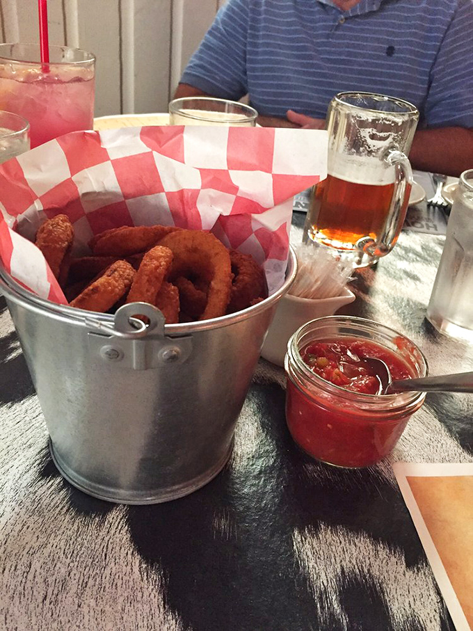 Golden-brown onion rings arrive in a silver bucket like treasure, accompanied by a cold beer and house-made sauce that makes ketchup seem like a sad afterthought.