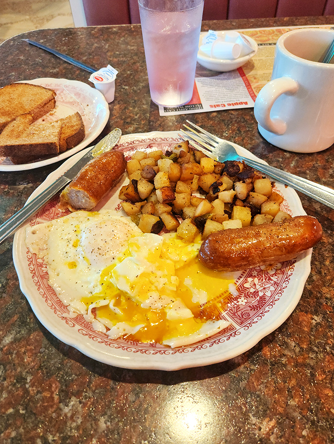 Breakfast perfection on a plate: sunny-side up eggs with golden yolks, crispy home fries, and sausage links that snap with each bite&mdash;the universal language of morning satisfaction.