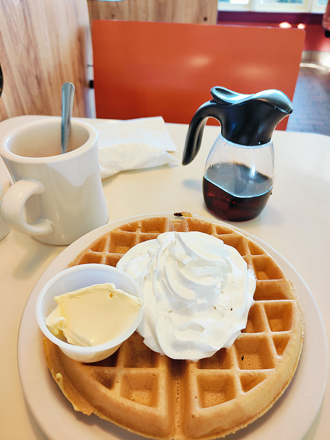 The Belgian waffle arrives like a throne for whipped cream royalty, waiting patiently with its perfect grid of syrup-catching squares.